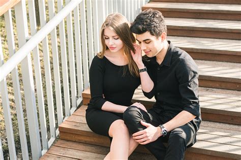 아름 다운 젊은 여러 인종 커플 사랑에 학생 부부는 도시에서 나무 계단을 앉아 있다 아름 다운 터키어 갈색 머리 남자가 검은 옷에 백인 여자를 포옹 화창한 날씨에 젊은이