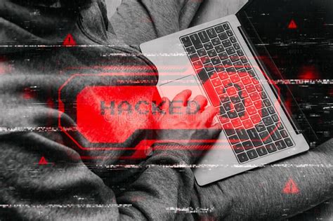 Hacker In A Hoodie Holds A Laptop With A Red Hacked Warning And Binary