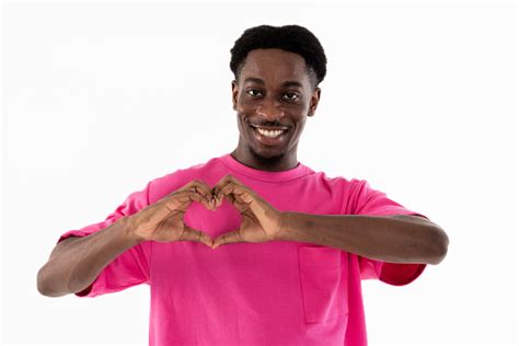 흰색 배경에 분홍색 티셔츠 유행 샷을 입고 심장 모양으로 팔을 잡고 좋은 분위기의 카메라를 바라보는 아프리카 남자의 초상화 갈색