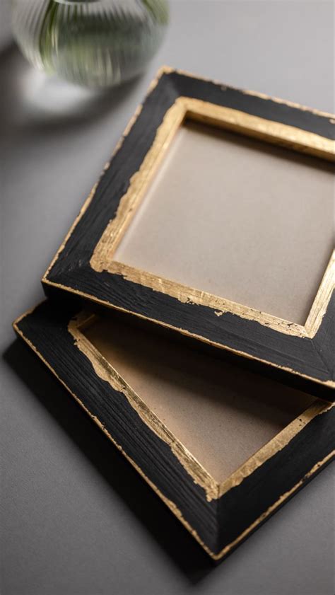 two black and gold frames sitting on top of a table next to a glass vase