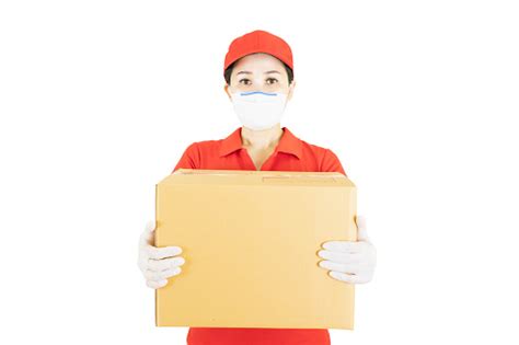 택배 나 딜러로 일하고 빨간 모자 의료 얼굴 마스크와 상자장갑을 착용 패키지를 제공하는 흰색 배경에 고립 된 빨간 유니폼을 입은