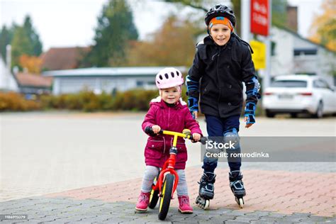 야외에서 함께 놀고있는 아이 소년과 어린 유아 소녀 롤러와 함께 스케이트 안전 의류에 형제 행복한 자매 자전거와 균형 자전거에 실행합니다 추운 날에 즐거운 시간을 보내는