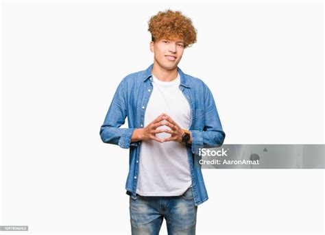 데님을 입고 아프로 머리를 가진 젊은 잘생긴 남자에는 손과 손가락을 엇갈리게 편안 하 고 밝은 미소 함께 자 켓 성공이 고