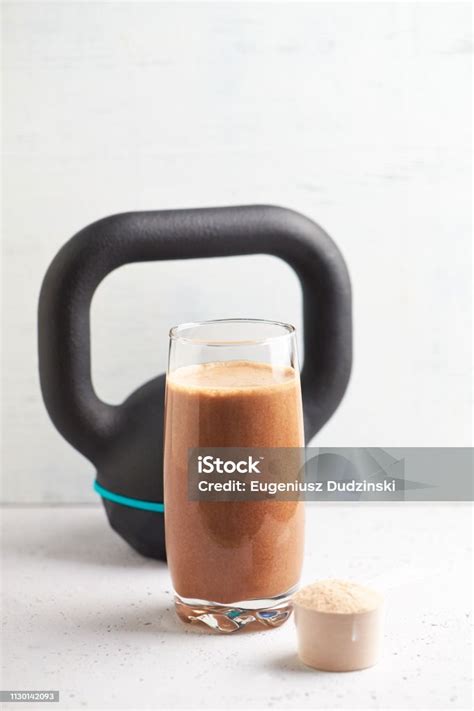밀크와 바나나가 함유 된 초콜릿 단백질 쉐이크 특 종 유 청 단백질 블랙 스포츠 케 틀 벨을 배경으로 한 컵 스포츠 영양 돌 나무 배경입니다 복사 공간 0명에 대한 스톡