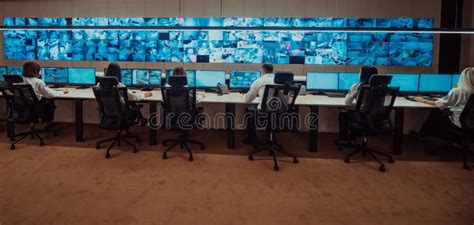 Group Of Security Data Center Operators Working In A Cctv Monitoring Room Looking On Multiple