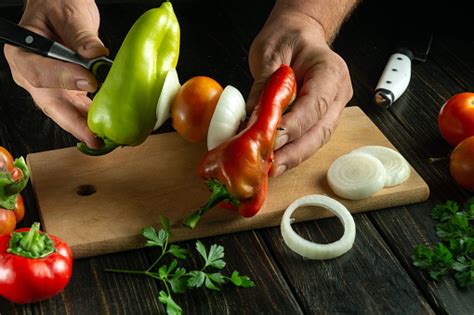 누군가 솜씨 좋게 고추 토마토 양파를 자르고 꼬치에 꿰습니다 신선한 허브와 추가 야채가 나무 도마를 둘러싸고 있어 준비 분위기를 더합니다 가위에 대한 스톡 사진 및 기타