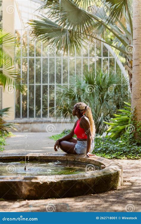 Verticale Di Una Donna Nera Con Le Trecce Bionde Seduta Vicino A Una Piccola Fontana Che Guarda