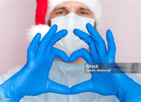 산타 모자 의료용 마스크 및 보호 장갑을 낀 의사는 심장의 상징을 보여줍니다 환자에 대한 의사 관리 및 사랑 개념 사랑 보살핌