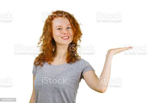 카메라를 보고 웃 고 회색 티셔츠에 곱슬 머리와 귀여운 빨간 머리 여자의 초상화 손 선물 또는 당신의 제품에 보여줍니다 흰색 배경에 고립 건강한 생활방식에 대한 스톡 사진