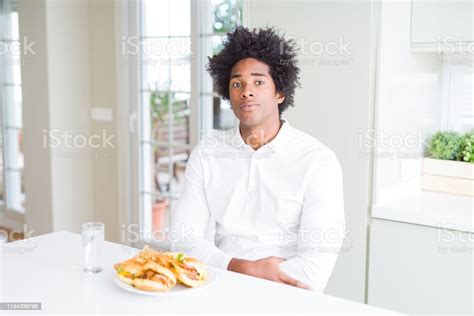 얼굴에 심각한 표정으로 점심 식사를 위해 햄버거를 먹는 아프리카계 미국인 배고픈 남자 카메라를 보고 간단 하 고 자연 스러운 가정 생활에 대한 스톡 사진 및 기타 이미지