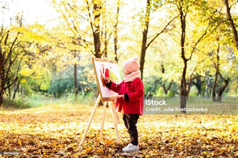 빨간 코트를 입은 어린 소녀가 가을 풍경을 배경으로 공원의 이젤에 수채화를 칠합니다 10월에 대한 스톡 사진 및 기타 이미지 10월 2 3 살 가을 Istock