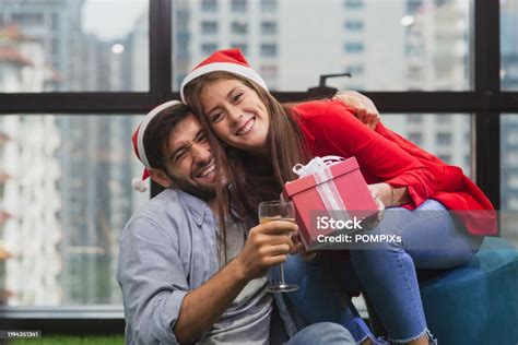 재미와 크리스마스 파티와 사랑에 젊은 커플 백인 잘 생긴 남자 들고 샴페인 유리 Ang 포옹 예쁜 여자 들고 선물 상자를 입고 산타 모자 축하 새해 파티 12월에 대한 스톡