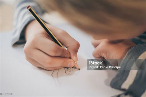 연필로 학생 그림의 보기를 닫습니다 종이에 숙제를 쓰는 소년 아이는 연필을 들고 집에서 만화를 그립니다 테이블에 앉아 십대