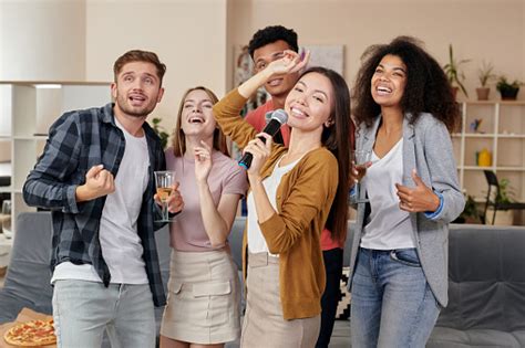 파티 재미 집에서 가장 친한 친구와 함께 노래방을 재생하는 동안 마이크를 들고 노래하는 젊은 아시아 소녀 술을 마시고 함께 즐거운 시간을 보내는 사람들의 그룹 18 19세에