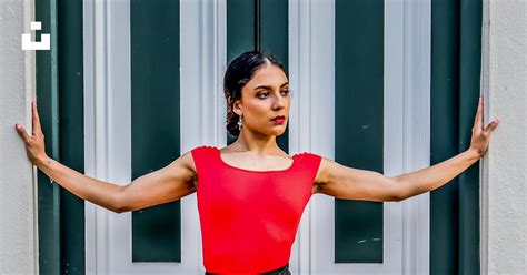 빨간 탱크 탑과 검은 치마를 입은 여자가 회색 나무 문 옆에 서 있다 사진 Unsplash의 무료 댄스 포즈 이미지