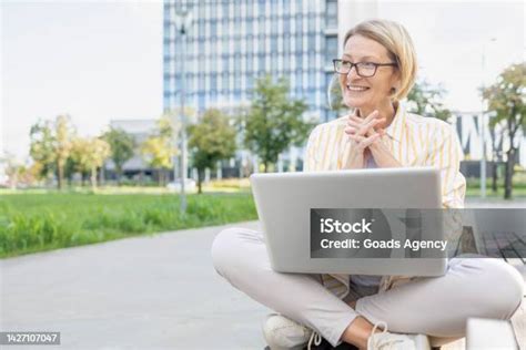공원 벤치에 앉아있을 때 노트북을 사용하는 흥분한 여성 50 54세에 대한 스톡 사진 및 기타 이미지 50 54세 55 59세 건물 외관 Istock