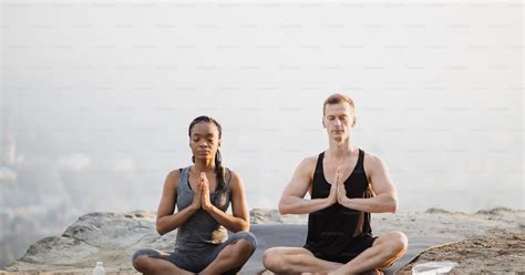 스포츠 옷을 입은 평화로운 다민족 커플이 연꽃 위치 요가 매트에 앉아 나마스테 손을 들고 있다 신선한 공기를 명상하는 동안 눈을 감고 있는 젊은 남녀 사진