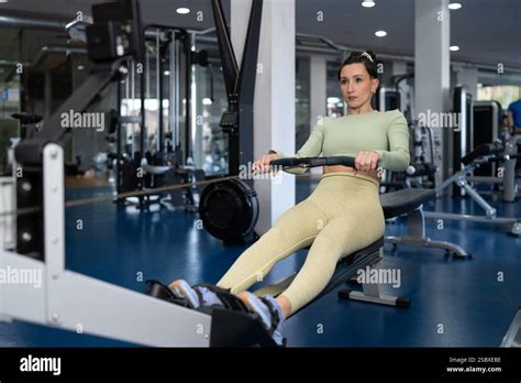 Focused Female Athlete Performing Rowing Exercise On A Fitness Machine Strengthening Back