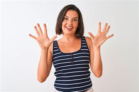 파란색 줄무늬 티셔츠를 입은 젊은 아름다운 여성은 자신감과 행복한 미소를 지으면서 손가락 번호 10을 보여주고 가리키는 고립 된 흰색 배경 위에 서 있습니다 T 셔츠에 대한