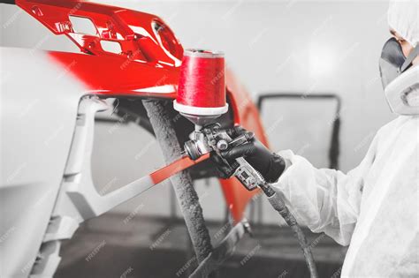 작업자는 스프레이 건으로 자동차 범퍼를 페인트합니다 수리 작업 중 페인트 챔버의 빨간 자동차 요소 사고 후 차량 복원