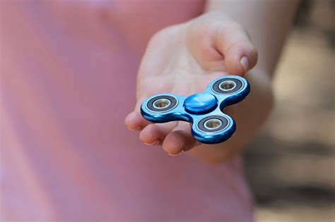 회색 배경 불안 릴리프 장난감에 인기 있는 피 젯 회전자 장난감을 들고 거리 여성 손에 손에 파란 금속 회전자를 재생 하는 여자