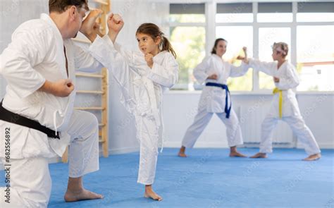 Focused Preteen Girl In White Kimono Practicing Karate Kicking Techniques During Sparring With