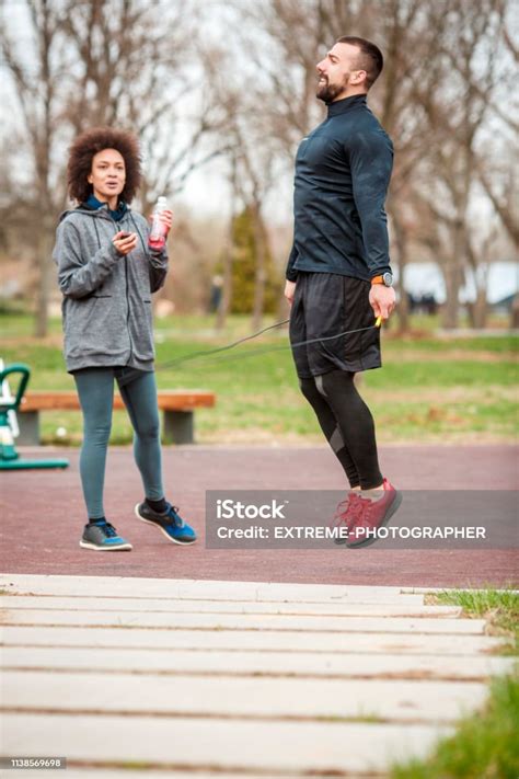그 옆에 서 있는 여성 피트 니스 강사와 함께 공원에서 점프 로프 운동을 하 고 있는 강한 운동 남자와 스톱 워치와 시간을 측정 2명에 대한 스톡 사진 및 기타 이미지