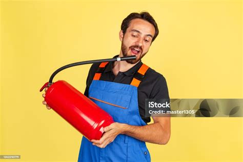 미소 짓는 젊은 수염을 기르는 남자 남성 자동차 정비사 또는 파란색 작업을 입은 피터의 반 길이 초상화가 노란색 스튜디오 배경에 고립되어 있습니다 유머에 대한 스톡 사진 및