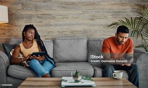 남자 친구가 그를 지켜보는 동안 거실에서 앉아서 기술을 사용하는 잘 생긴 젊은 남자의 샷 간통에 대한 스톡 사진 및 기타 이미지 간통 의심 커플 Istock