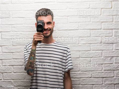 치아를 보여주는 자신감 미소로 웃 고 행복 한 얼굴 서 흰색 벽돌 벽을 통해 서에 비디오 카메라를 들고 촬영 하는 젊은 남자 건강한 생활방식에 대한 스톡 사진 및 기타