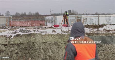 건설 현장의 수평 및 수직 평면의 각도를 측정하기 위해 테오돌라이트 측량 광학 기기를 사용하는 건설 작업자두 명의 엔지니어가 건설 현장에서 측정합니다 측지학에 대한 스톡