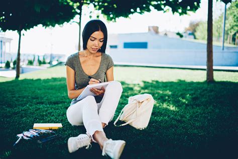 매력적인 갈색 머리 여자 캐주얼 착용에 녹색 잔디에 앉아 숙제를 하 고 화창한 날 동안 대학 캠퍼스에서 창조적 인 작업을 완료 메모장에 스케치를 만드는 여학생 갈색 머리에