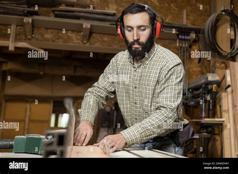 Horizontal Photo Serious Carpenter With Hearing Protection Operates A Table Saw Pushing A