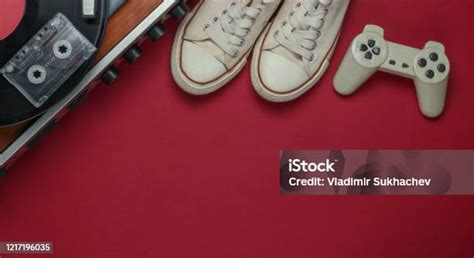 플랫 누워 복고풍 미디어 및 엔터테인먼트 비닐 레코드 오디오 카세트 게임 패드 빨간색 배경에 운동화와 비닐 레코드 플레이어 공간을 복사합니다 80년대 탑 뷰 0명에 대한