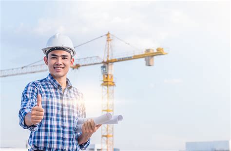 엔지니어의 백색 안전 헬멧을 착용 누르고 건설 사이트 및 크레인 배경으로 청사진 그는 그의 프로젝트 성공 때문에 미소를가지고 건설 현장에 대한 스톡 사진 및 기타 이미지