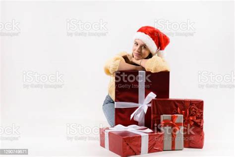 빨간 종이에 싸인 선물 상자 근처에 앉아 있는 젊은 아름다운 Lwoman 빨간 산타 모자를 쓰고 흰색 배경에 고립 된 흰색 활 25 29세에 대한 스톡 사진 및 기타 이미지