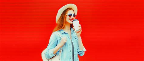 여름 밀짚 둥근 모자를 쓰고 커피 한 잔을 들고 행복한 미소 짓는 젊은 여성의 초상화 빨간색 배경에 배낭이있는 데님 재킷 광고 텍스트를위한 빈 복사 공간 20 29세에 대한