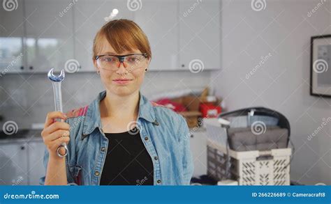 Young Woman With Safety Glasses Holding A Spanner Upwards In The Kitchen Tools In The