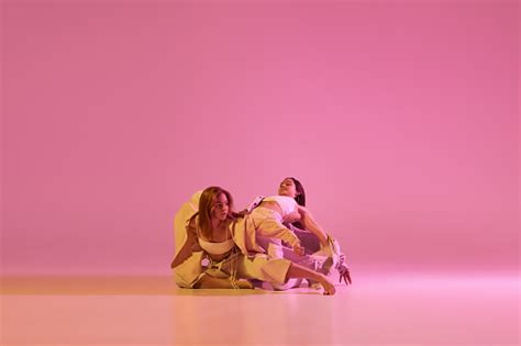 캐주얼 스타일의 옷을 입은 두 명의 세련된 여성 댄서가 크리스탈 핑크 배경 위에 현대 안무 춤을 추고 있습니다 현대 미술 창의성