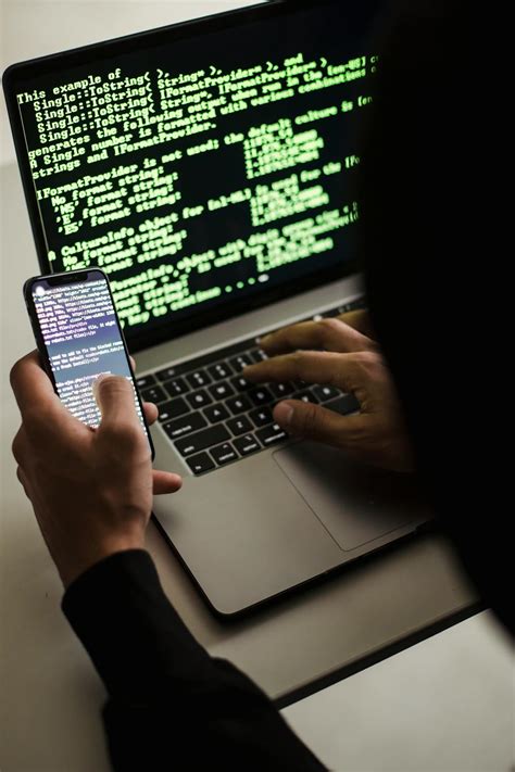 unrecognizable hacker with smartphone typing on laptop at desk · free