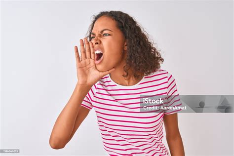 분홍색 줄무늬 티셔츠를 입은 젊은 브라질 여성이 고립된 흰색 배경 위에 서서 입을 다물로 큰 소리로 외치고 비명을 지르고 있습니다 통신 개념입니다 T 셔츠에 대한 스톡 사진