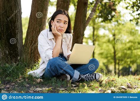 Portrait Of Young Asian Woman Sitting In Park Near Tree Working On