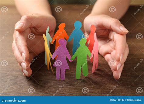 woman protecting paper human figures on wooden table closeup