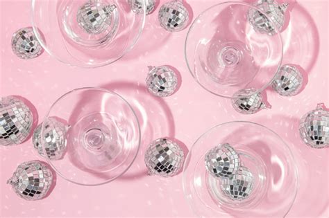 마티니와 마가리타 칵테일 잔과 파스텔 핑크 배경에 디스코 볼 장식이 있는 크리스마스 파티 창의적인 레이아웃 복고풍 패션 미적 파티 개념 트렌디 한 새해 또는 크리스마스 휴가