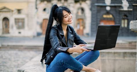 행복한 힙스터 젊은 혼혈 여성이 도시에서 노트북으로 작업하고 있다 포니테일 머리를 한 사랑스러운 아시아 여성 빈티지 돌 분수에 앉아 공부하고 노트북 사용 사진