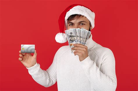 잘 생긴 힙스터 남자는 빨간 배경에 얼굴을 덮고 신용 카드와 현금 돈을 들고 산타 클로스 모자를 착용 12월에 대한 스톡 사진 및 기타 이미지 Istock