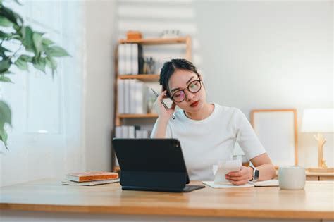 안경을 쓴 여자가 책과 아늑한 램프에 둘러싸인 태블릿을 들고 영수증을 들고 생각에 잠겨 책상에 앉아 있습니다 25 29세에 대한 스톡 사진 및 기타 이미지 Istock