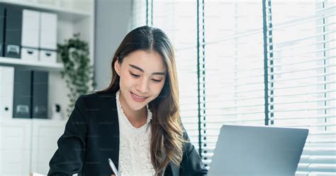 공식적인 정장을 입은 아시아의 행복한 아름다운 사업가는 직장에서 일합니다 매력적인 여성 직원 사무원 미소 노트북 컴퓨터를 사용하여 동료와 토론하고 회사에서 종이에