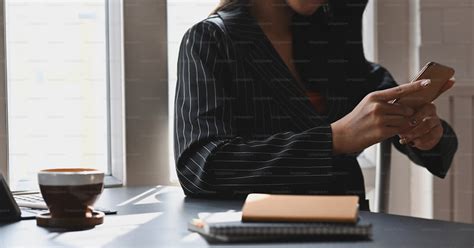 편안한 거실 위의 작업 책상에 앉아 있는 동안 손에 스마트폰을 들고 있는 매력적인 사업가의 자른 이미지 사진 Unsplash의 홈 인테리어 이미지