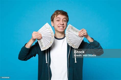 달러 지폐에 돈의 팬을 들고 캐주얼 복장에 즐거운 젊은 남자를 웃 고 스튜디오에서 파란색 배경에 고립 된 현금 돈 사람들은 진심으로 감정 라이프 스타일 개념입니다 복사